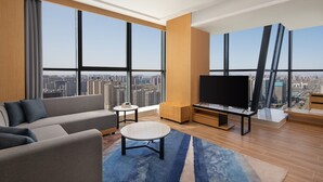 Uma sala de estar moderna com uma televisão grande, um sofá, uma mesa de centro e vista para a paisagem urbana através de grandes janelas.