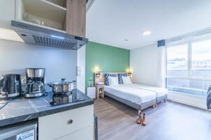 Quarto de hotel moderno com cama, uma kitchenette pequena, janela com vista para a cidade e teto de madeira.