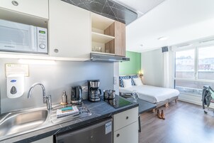 Cozinha moderna com micro-ondas, cafeteira e pia. Há uma cama com vista para a cidade.
