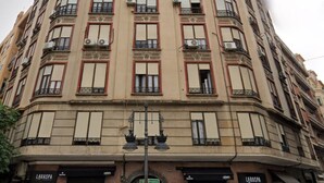 Edifício de vários andares com estilo arquitetônico clássico, apresentando uma entrada central com porta preta e uma placa acima.
