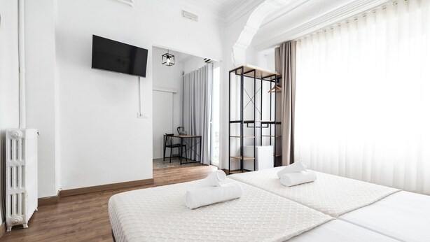 Quarto de hotel com duas camas, televisão, secretária e janela com cortinas.