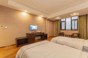Quarto de hotel com duas camas, uma mesa de trabalho com televisão, uma janela com cortinas e vista para a cidade.