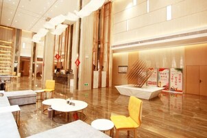 Um hall amplo com teto alto, área de estar central com mesa redonda e balcão de recepção.