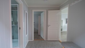 Entrada de uma cabana com um banco, soalho ladrilhado e portas brancas que dão para outros espaços.