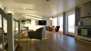 Uma sala de estar ampla com uma mesa de jantar, cadeiras, um sofá e uma TV fixada na parede.