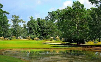 Um campo de golfe com lago, árvores e bunkers de areia.