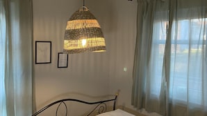 Quarto com cama, luminária pendente e cortinas finas.