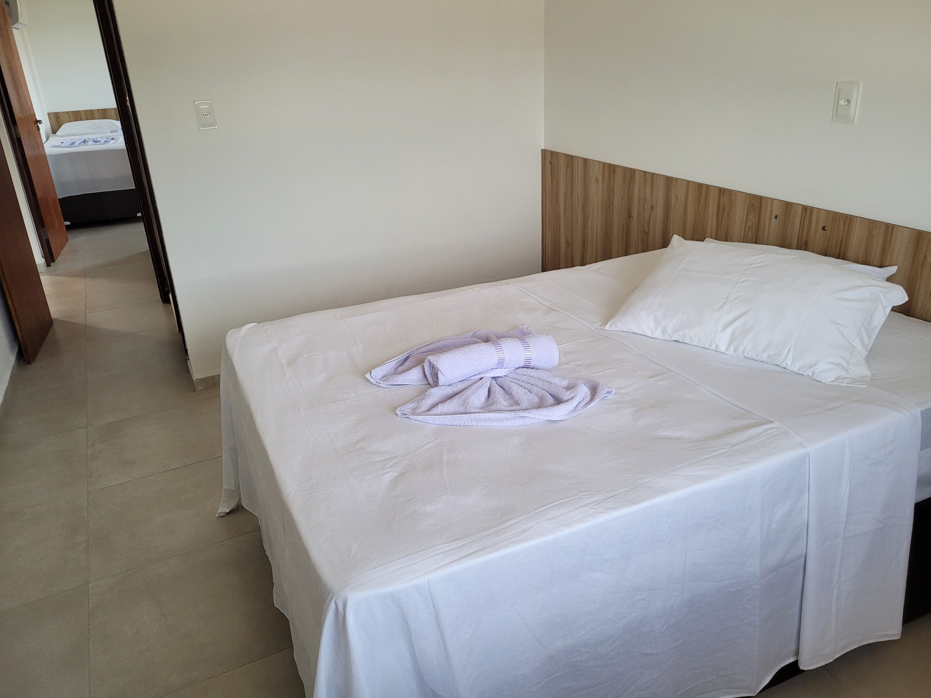 Cama bem arrumada com roupa branca e uma toalha dobrada.
