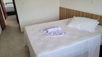 Cama bem arrumada com roupa branca e uma toalha dobrada.