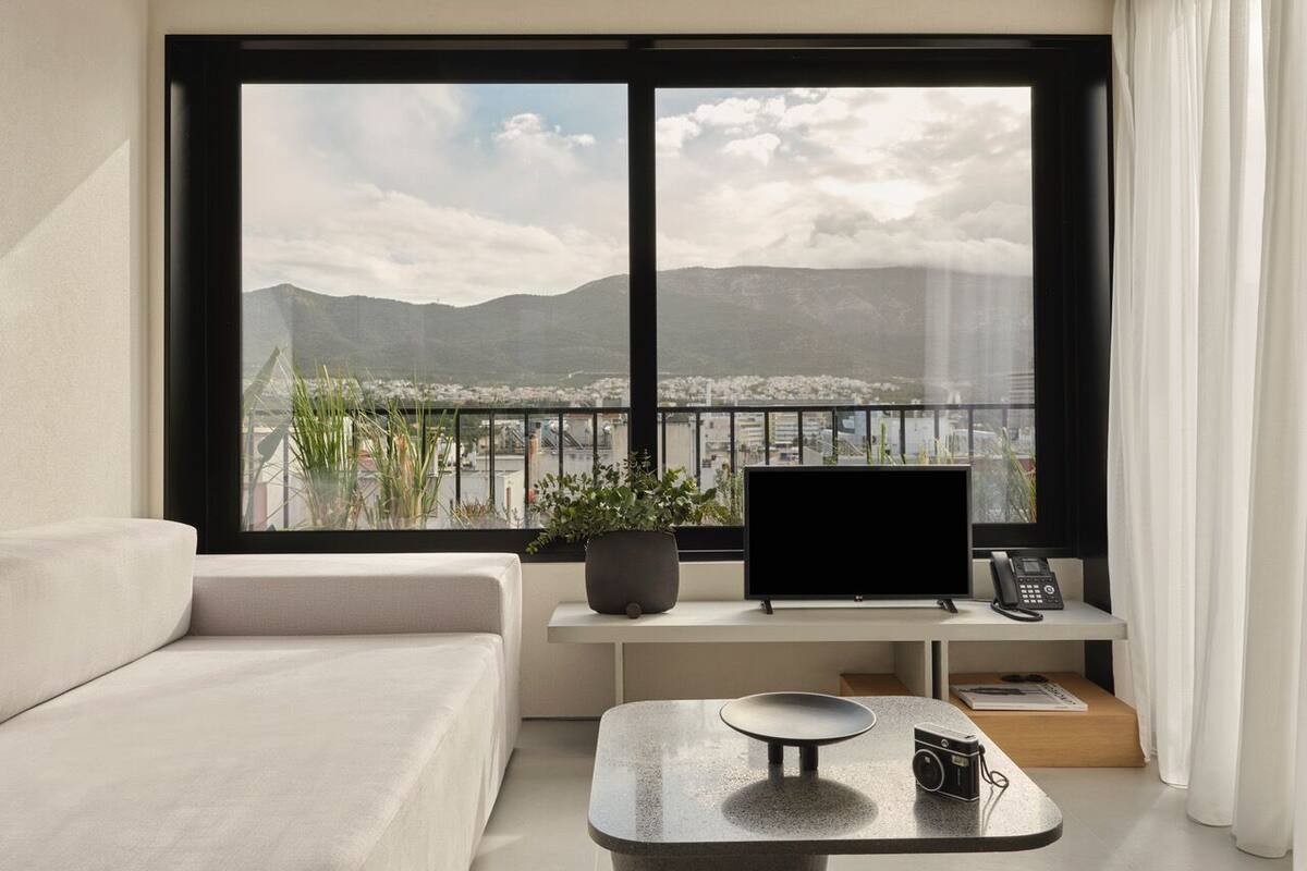Uma sala de estar moderna com uma janela ampla, um sofá, uma mesa de centro, uma televisão, uma planta e vista para uma varanda.