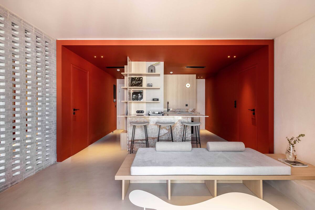 Quarto de hotel moderno com design minimalista, com uma cama, uma pequena cozinha e um espaço de estar com bancos.
