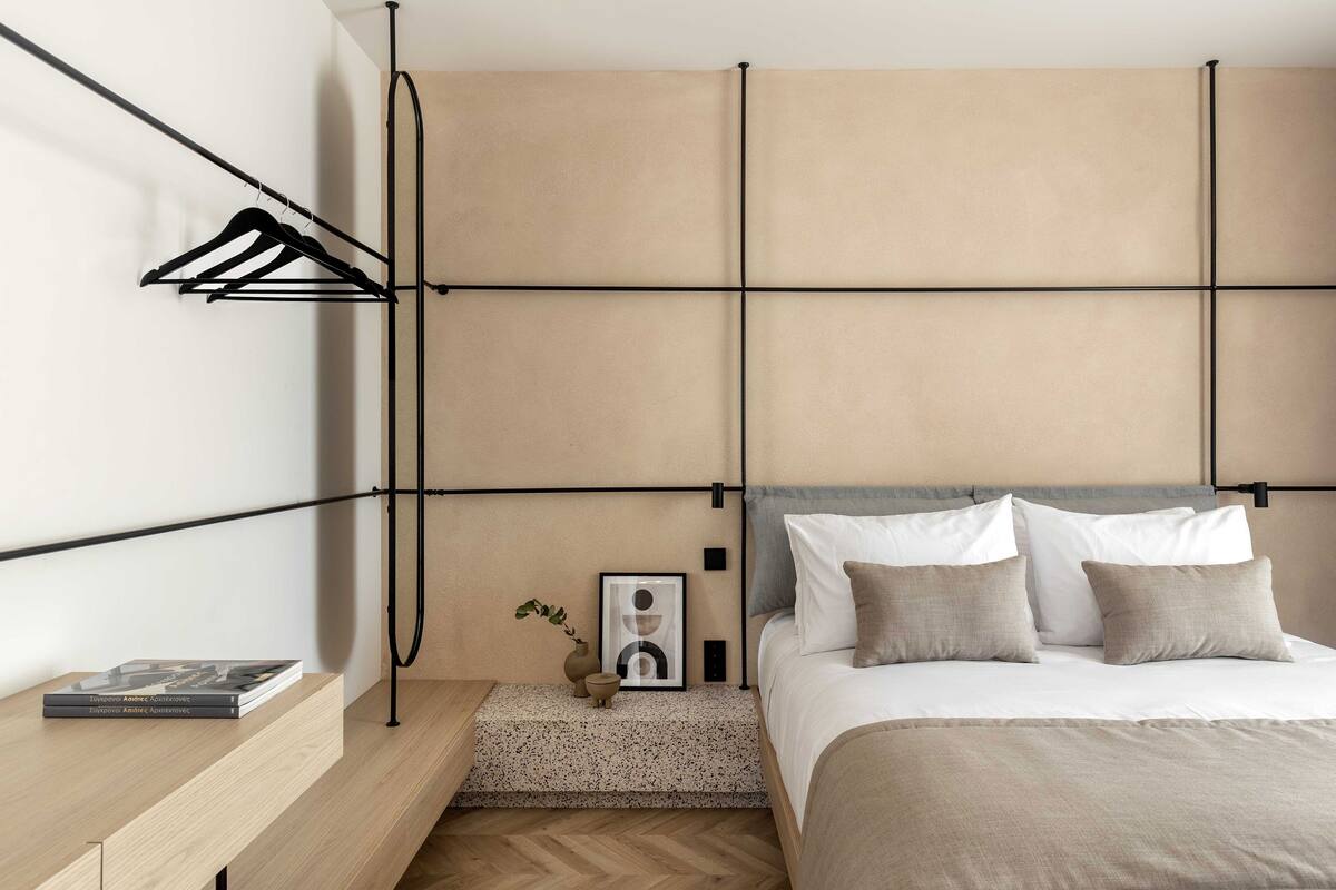 Quarto moderno com cama, mesa de cabeceira, prateleira na parede e cabideiro.