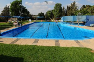 Piscina retangular com divisórias de pistas, rodeada por um deck ladrilhado e gramado.
