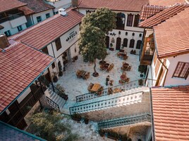 Vista aérea de um pátio com mesas ao ar livre, uma escadaria e um edifício com telhado de azulejos.