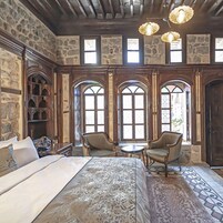 Um quarto com uma cama grande, duas poltronas, uma mesa pequena e uma parede de pedra com janelas em arco.