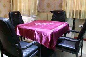 Uma sala de jantar com uma mesa coberta por toalha vermelha, quatro cadeiras pretas e uma janela com cortinas.