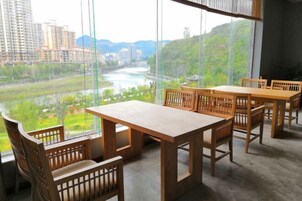 Uma sala de jantar com mobiliário de madeira e grandes janelas que oferecem vista para um rio e vegetação ao redor.