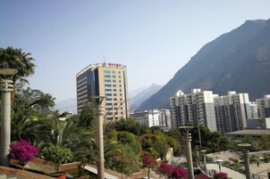 Um edifício alto com vários andares, cercado por vegetação exuberante e uma montanha ao fundo.