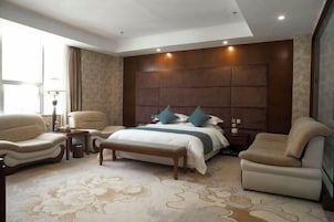 Quarto de hotel com uma cama grande, duas poltronas, um banco de madeira e um tapete decorativo.