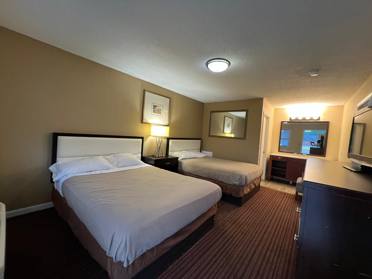 Quarto de hotel com duas camas, uma escrivaninha, uma cômoda e uma televisão.