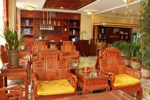 Disposição tradicional de móveis de madeira com cadeiras e mesas, rodeada por estantes de livros e plantas em vasos.