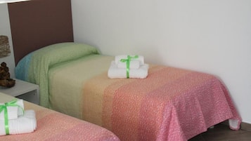 Quarto de hotel com duas camas, cada uma com um edredom de cor diferente, e um par de toalhas dobradas com um laço verde.