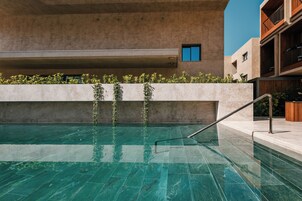 Uma área de piscina moderna com superfície de água cristalina, parede de concreto com vegetação e varanda de madeira.