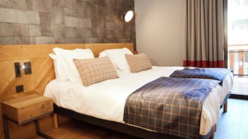 Uma cama de casal com manta xadrez, cabeceira de madeira e mesa de cabeceira com abajur.