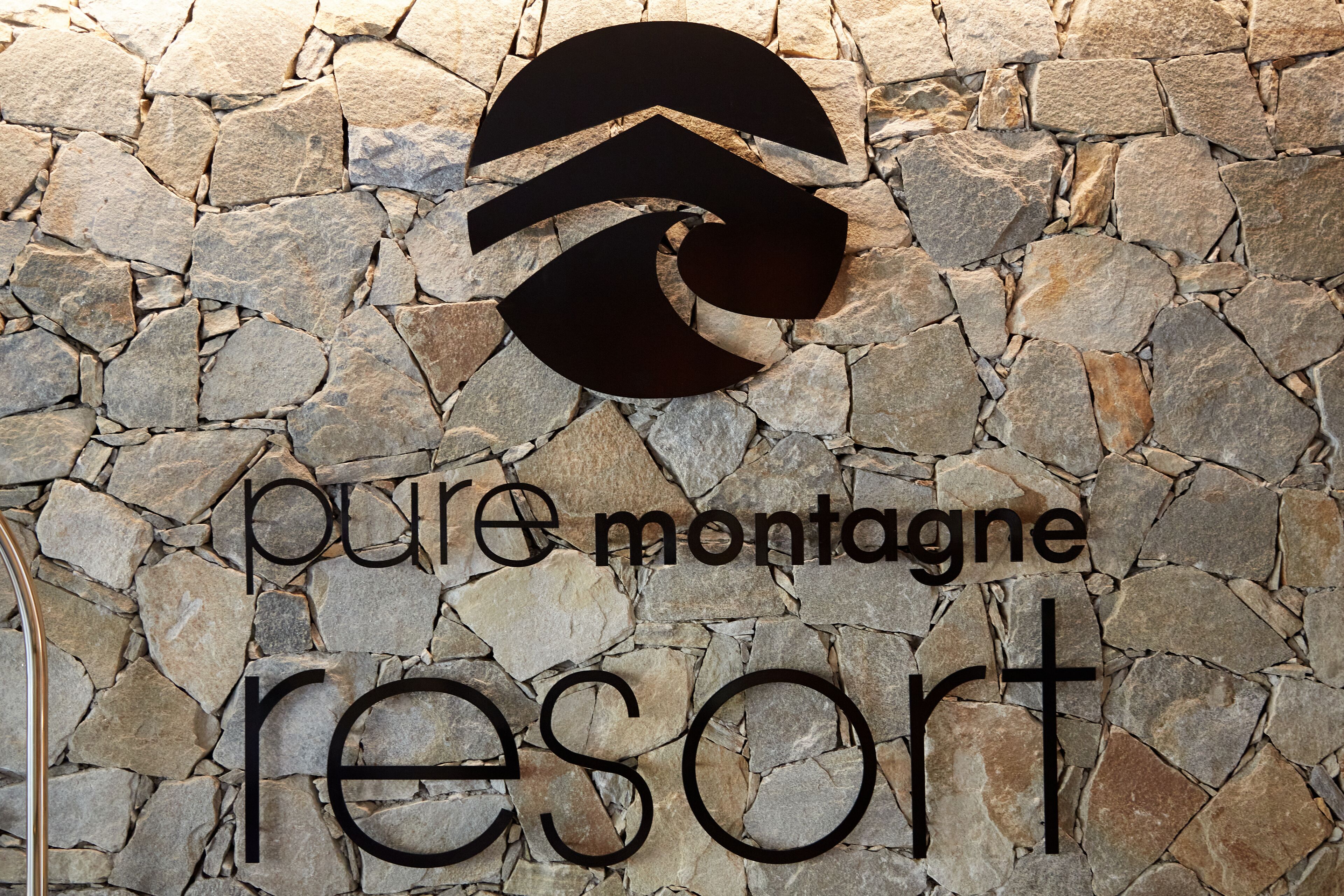 Um muro de pedra com o texto "pure montagne resort" e um logotipo acima.