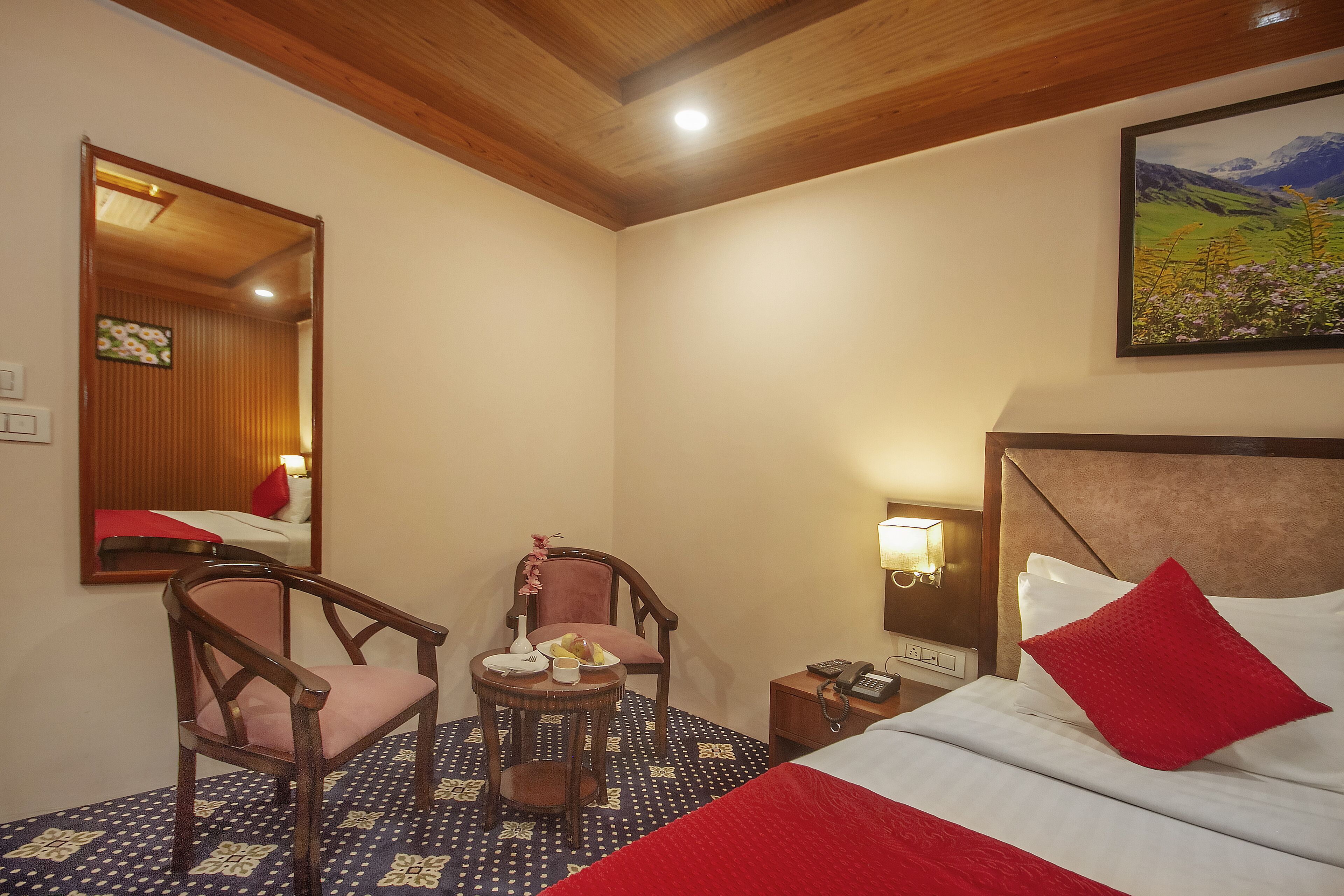 Quarto de hotel com cama, uma cadeira, uma pequena mesa com um prato de comida, um espelho e um quadro na parede.