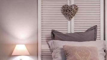 Cama bem arrumada com edredom branco, luminária de cabeceira e mesa de apoio com um vaso.