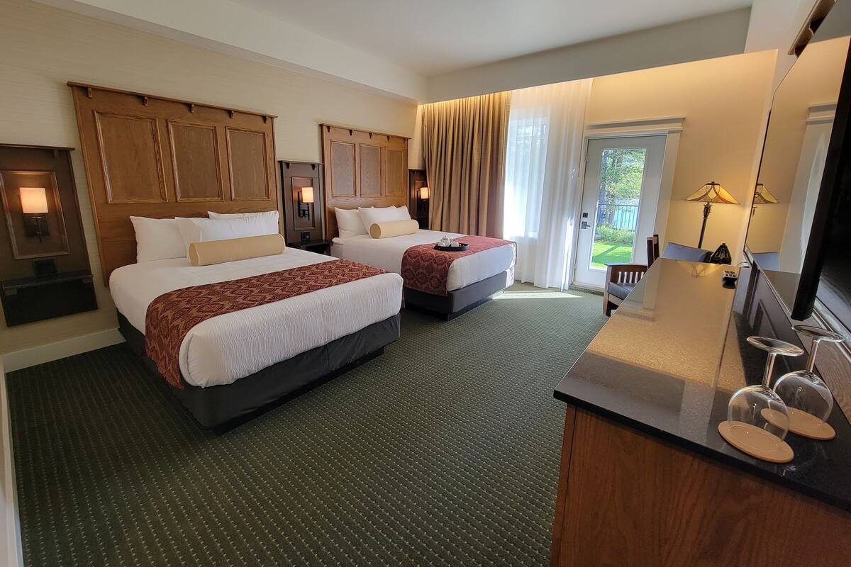Quarto de hotel com duas camas, uma escrivaninha, um espelho e uma porta de vidro deslizante para o exterior.