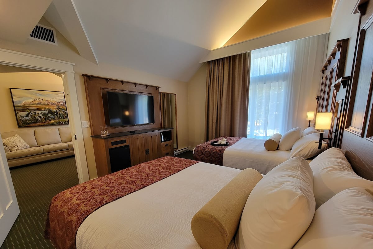Quarto de hotel com duas camas, televisão, pintura e janela com cortinas.