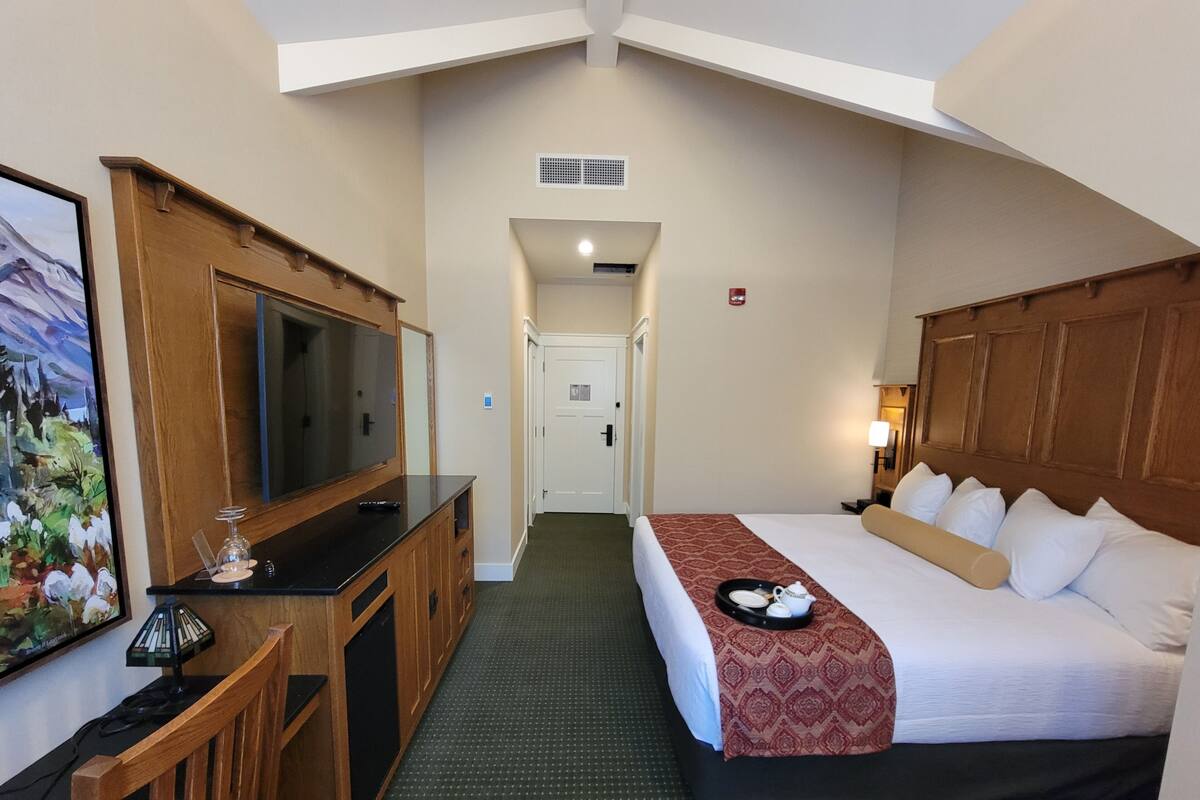 Quarto de hotel com cama, televisão, escrivaninha e um quadro na parede.