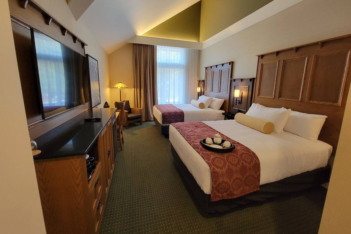 Quarto de hotel com duas camas, uma escrivaninha, uma televisão e um abajur.