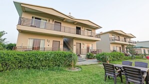 Um edifício residencial de dois andares com varandas, uma escadaria e um jardim bem cuidado com uma mesa e cadeiras.