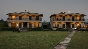 Um edifício de dois andares com telhado plano, escadaria que dá acesso ao andar superior e um gramado bem cuidado.