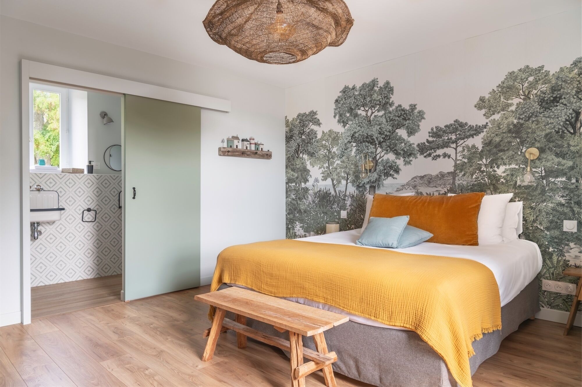 Quarto com cama, um banco, um mural na parede e uma janela.