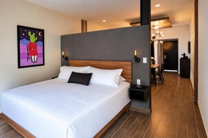 Quarto de hotel com uma cama grande, uma mesa de cabeceira, uma luminária na parede e um quadro.
