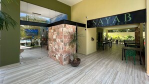 Interior moderno com um pilar de pedra, placa de restaurante e área de estar ao ar livre visível através de paredes de vidro.