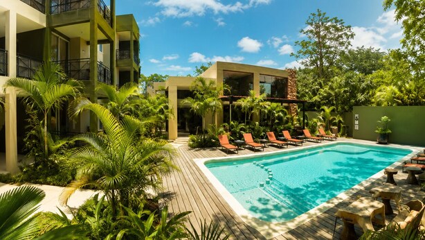 Um hotel moderno com piscina, espreguiçadeiras e plantas tropicais.