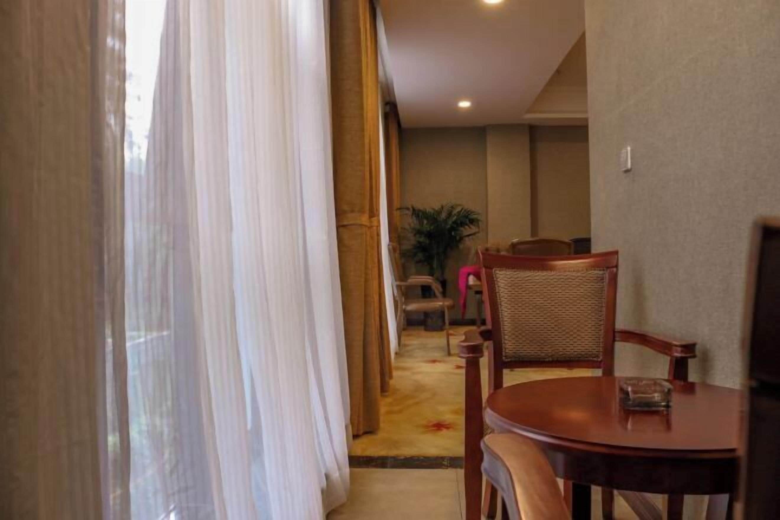 Corredor de hotel com uma cadeira e mesa de madeira, uma planta e uma cortina.