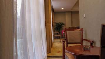 Corredor de hotel com uma cadeira e mesa de madeira, uma planta e uma cortina.