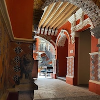 Interior com escadaria que leva a um andar superior, colunas ornamentadas e uma estátua de leão.
