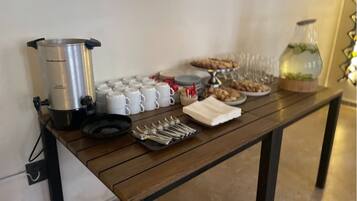 Uma mesa de buffet com uma máquina de café, pratos, copos e um vaso decorativo.