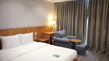 Quarto de hotel com cama, escrivaninha, cadeira, mesinha e abajur.