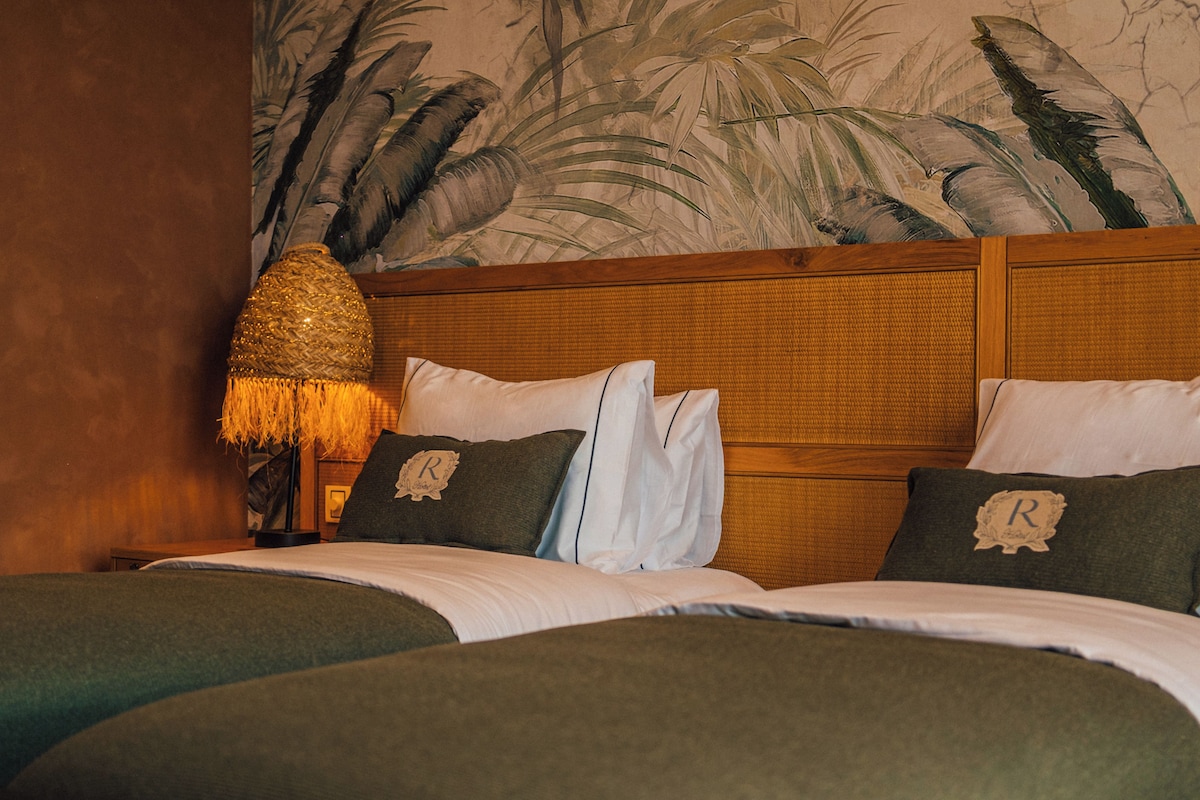 Quarto de hotel com duas camas, cabeceira de madeira e um mural tropical na parede.