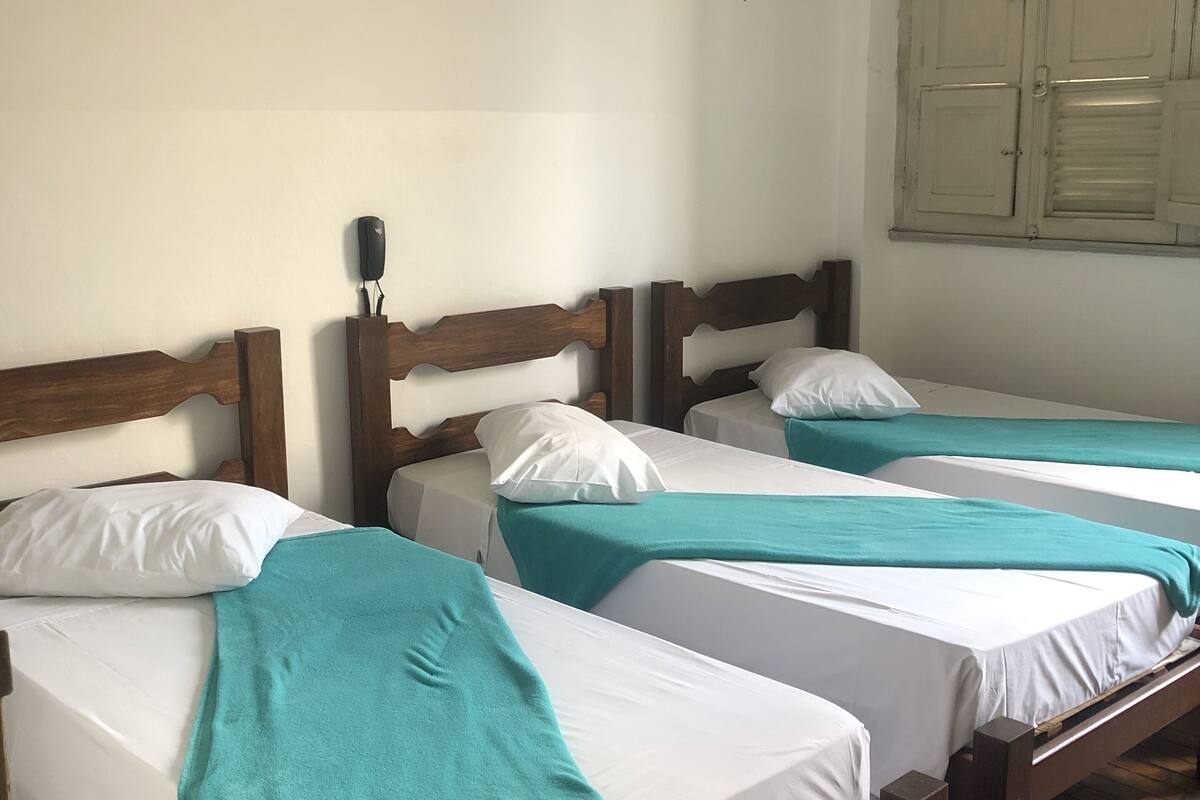 Quarto com três camas de madeira, cada uma com roupa de cama branca e cobertores verde-água.