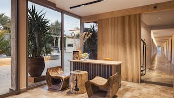 Uma área de recepção moderna com um balcão de madeira, duas cadeiras de madeira, uma grande planta em vaso e vista para o exterior.