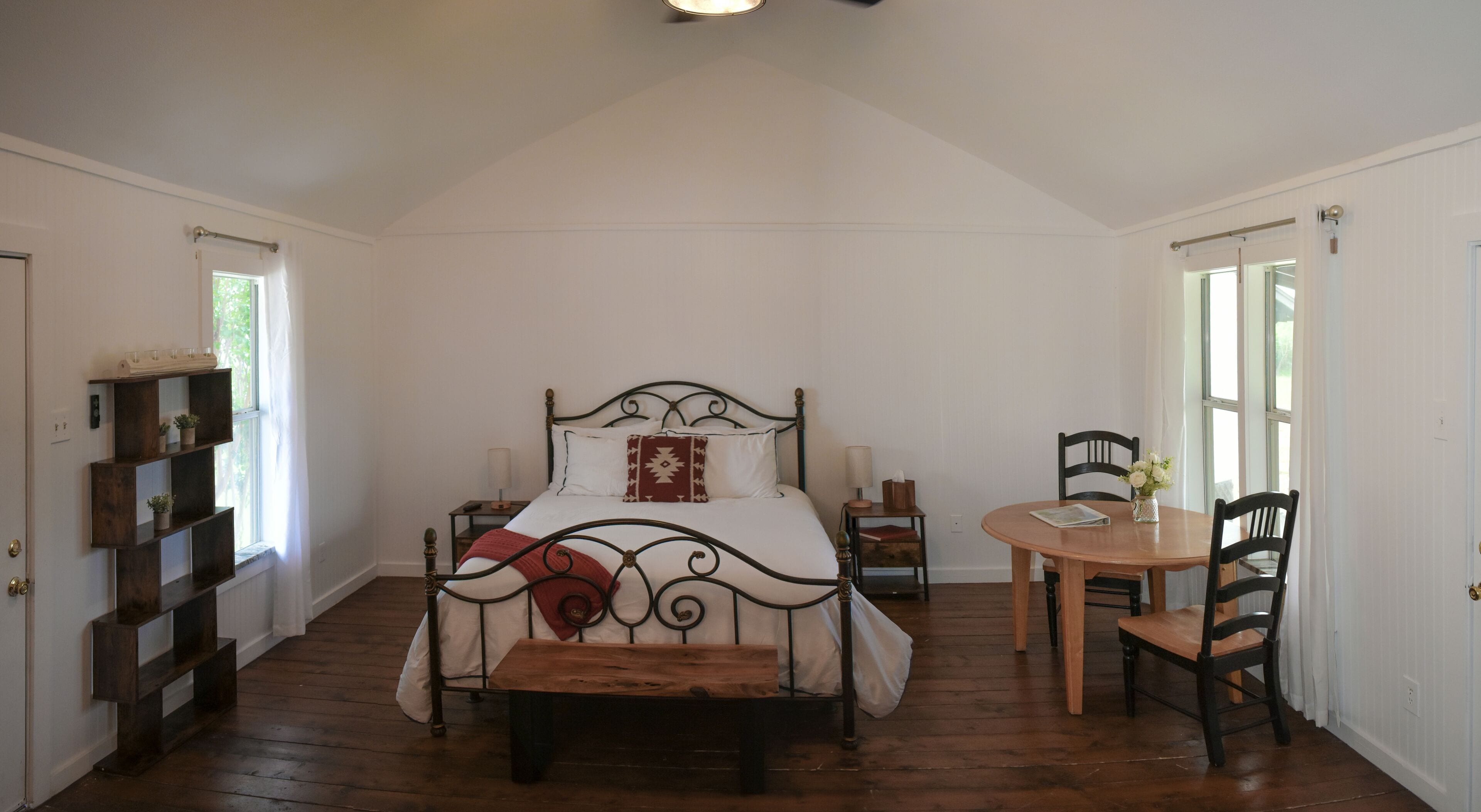 Um quarto com cama, um banco de madeira, uma mesa com cadeiras e uma estante de livros.